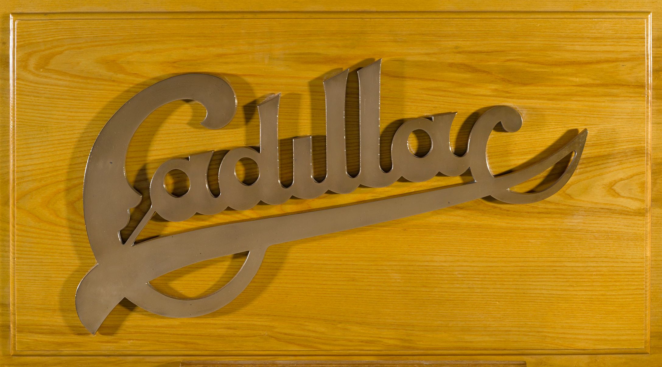 Bonhams Cars : A brass "Cadillac" sign mounted on wood,